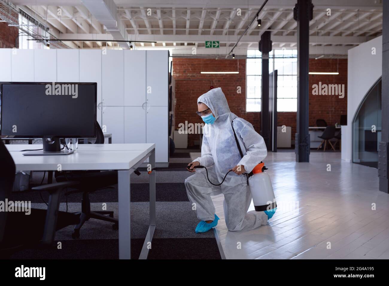 Cleaner wearing ppe suit, glasses and mask disinfecting office ...