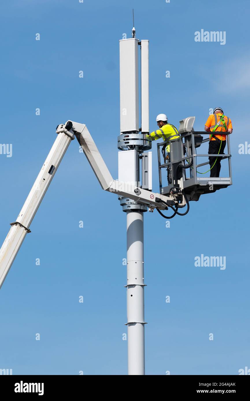 Workers install a 5G mobile phone transmitter using a cherry picker ...
