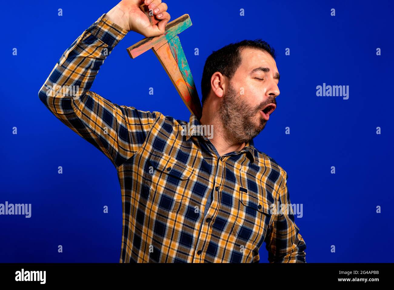 Bearded man in a yellow plaid shirt scratching his back with a wooden ...