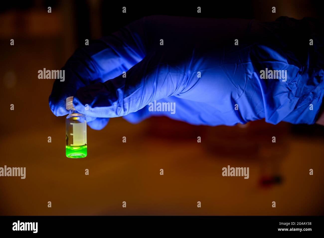 Scientist holding a green colour solution in a glass vial wearing a ...