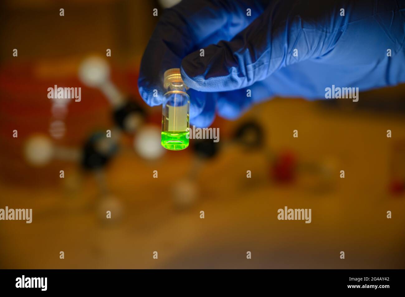 Scientist holding a greeen colour solution in a glass vial wearing a ...