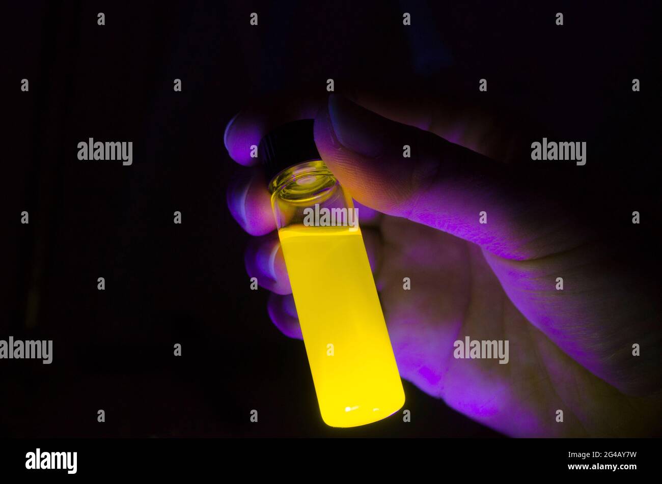 Woman researcher holding yellow photochemical reaction in glass vial ...