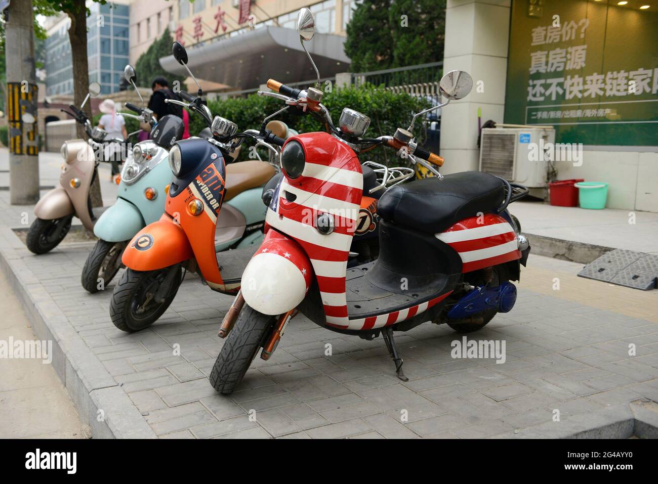 Four brightly coloured motor scooters parked in a line on a pavement in ...