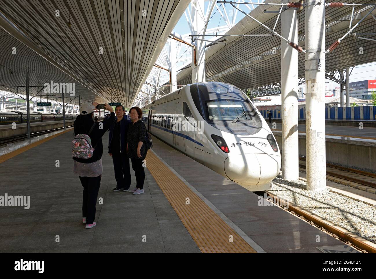 A group of travelers take a photo in front of a high speed train at ...