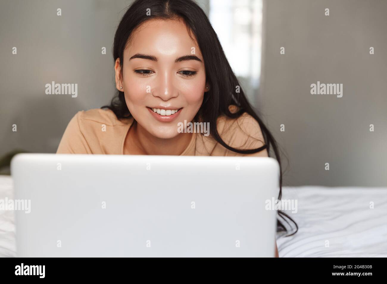 Portrait of young asian woman working with laptop from bed, lying in ...