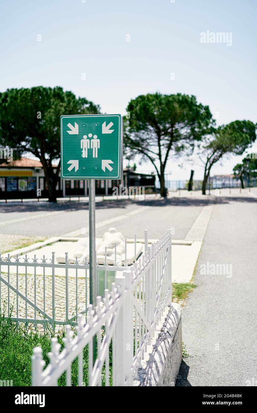 Evacuation sign behind a metal fence in a green park. Sign: Assembly ...