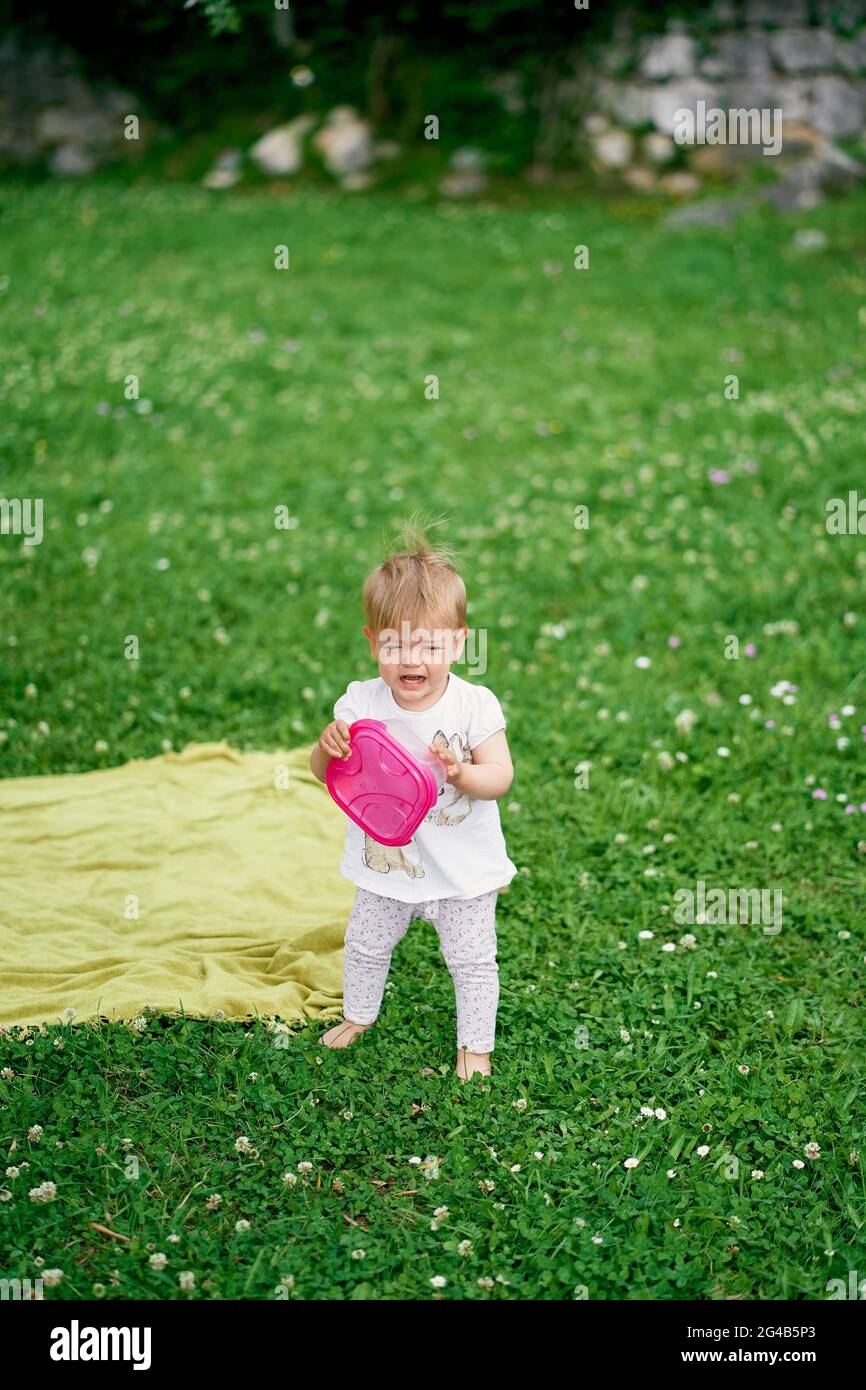 Whimpering child stands on a green lawn and holds a plastic food ...