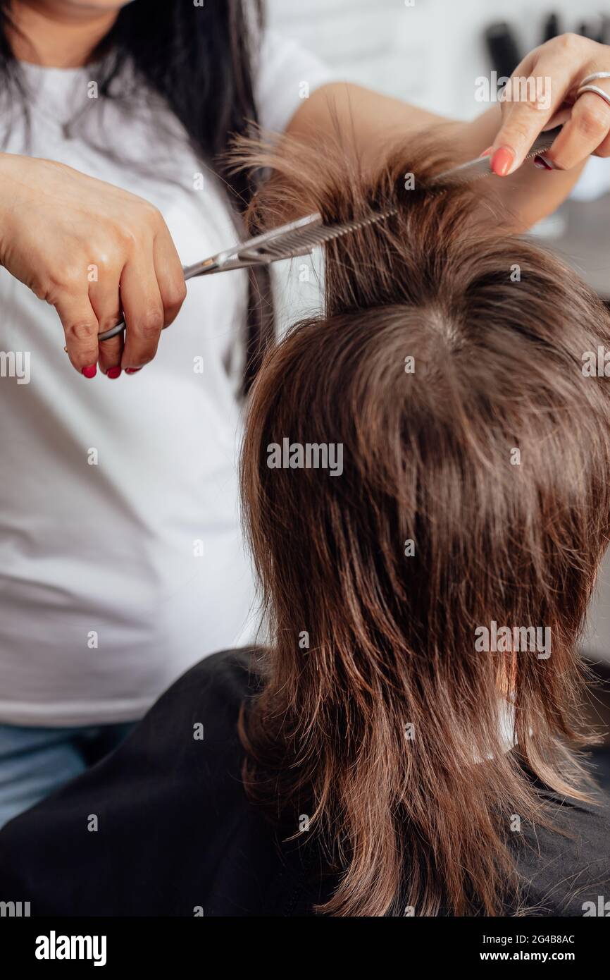Woman getting a new haircut. Female hairstylist cutting her long black ...