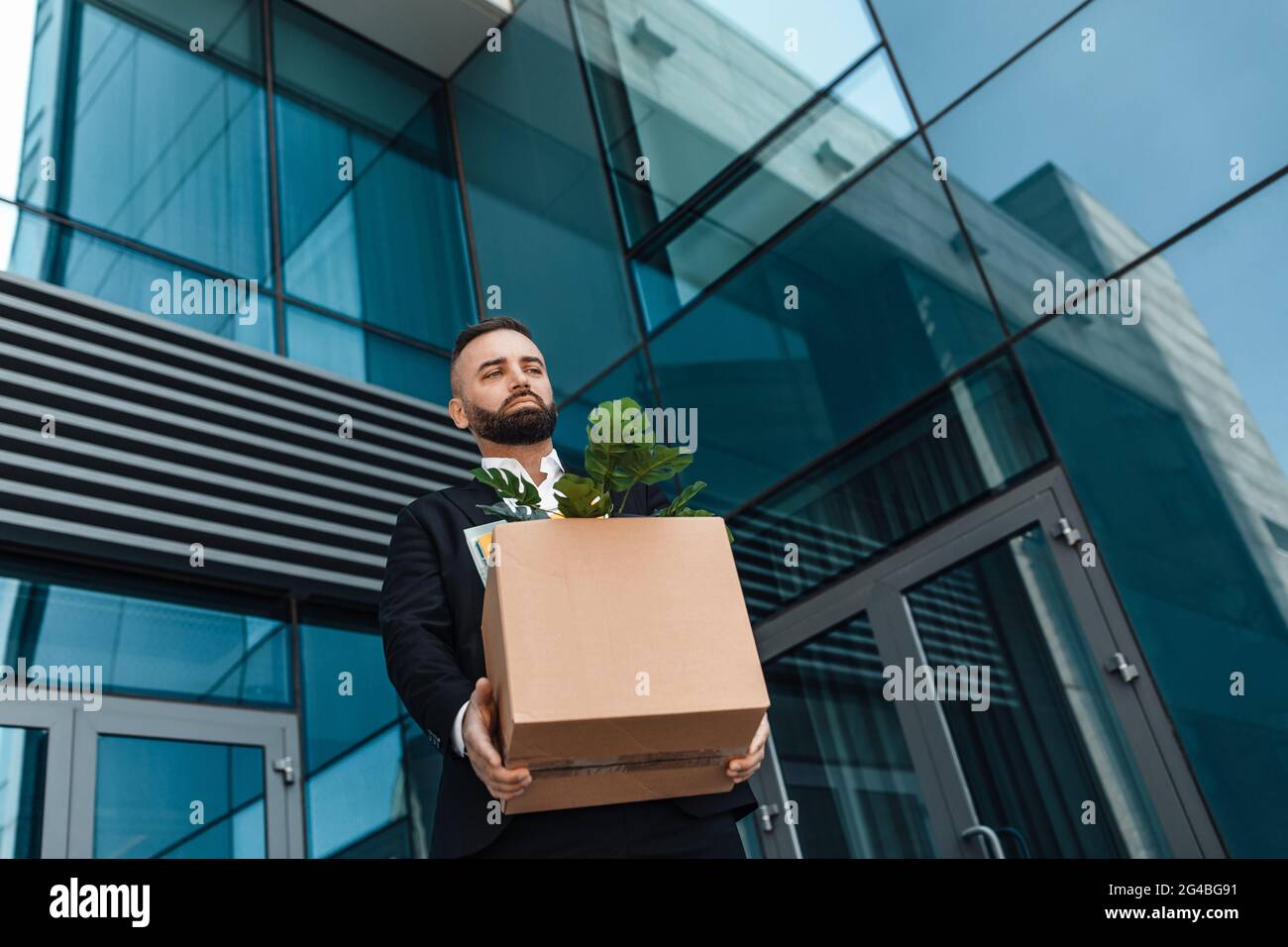 Fired depressed male office worker with box of personal stuff walking ...