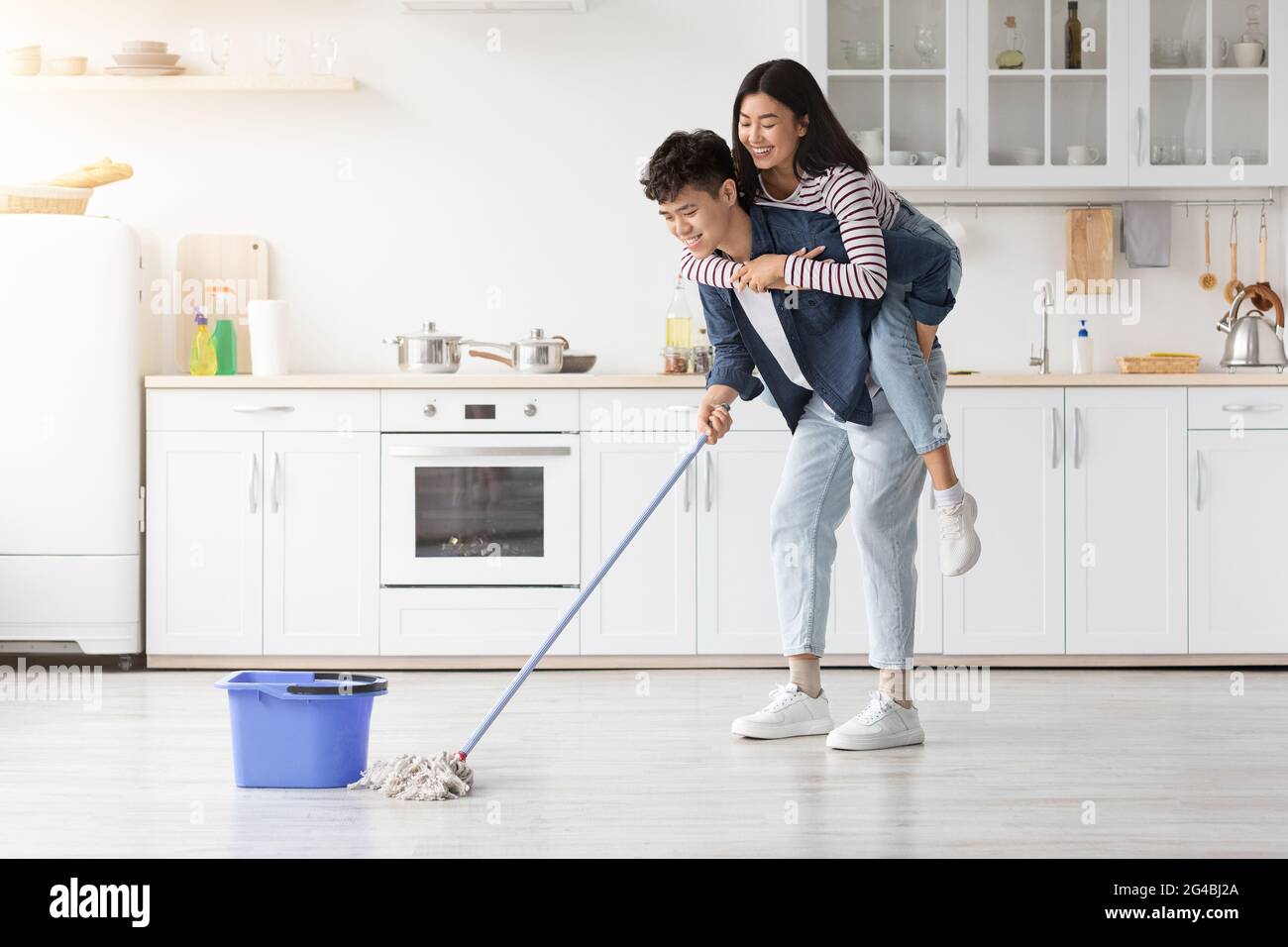 Cheerful asian guy piggyback his pretty girlfriend while mopping ...