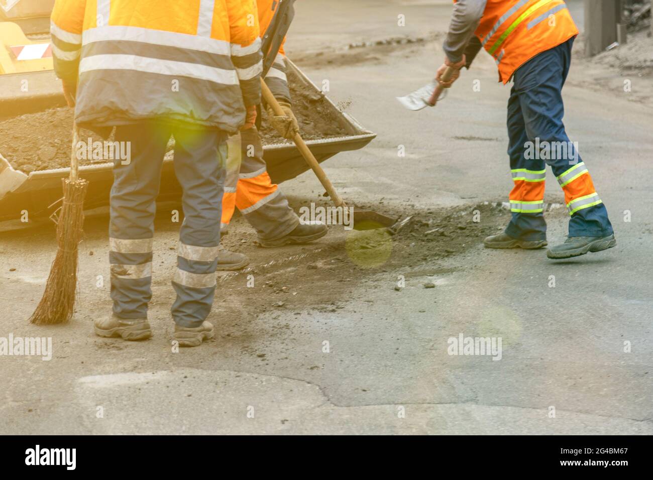 Road workers in bright orange reflective uniforms use shovels to scrape ...