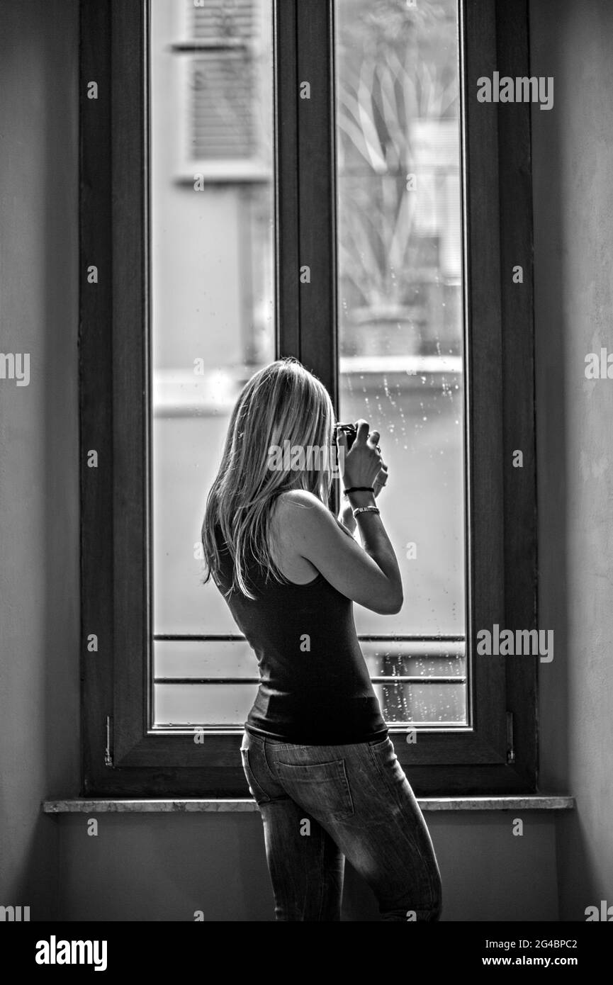 a grayscale shot of a young female taking a shot from a tall window ...