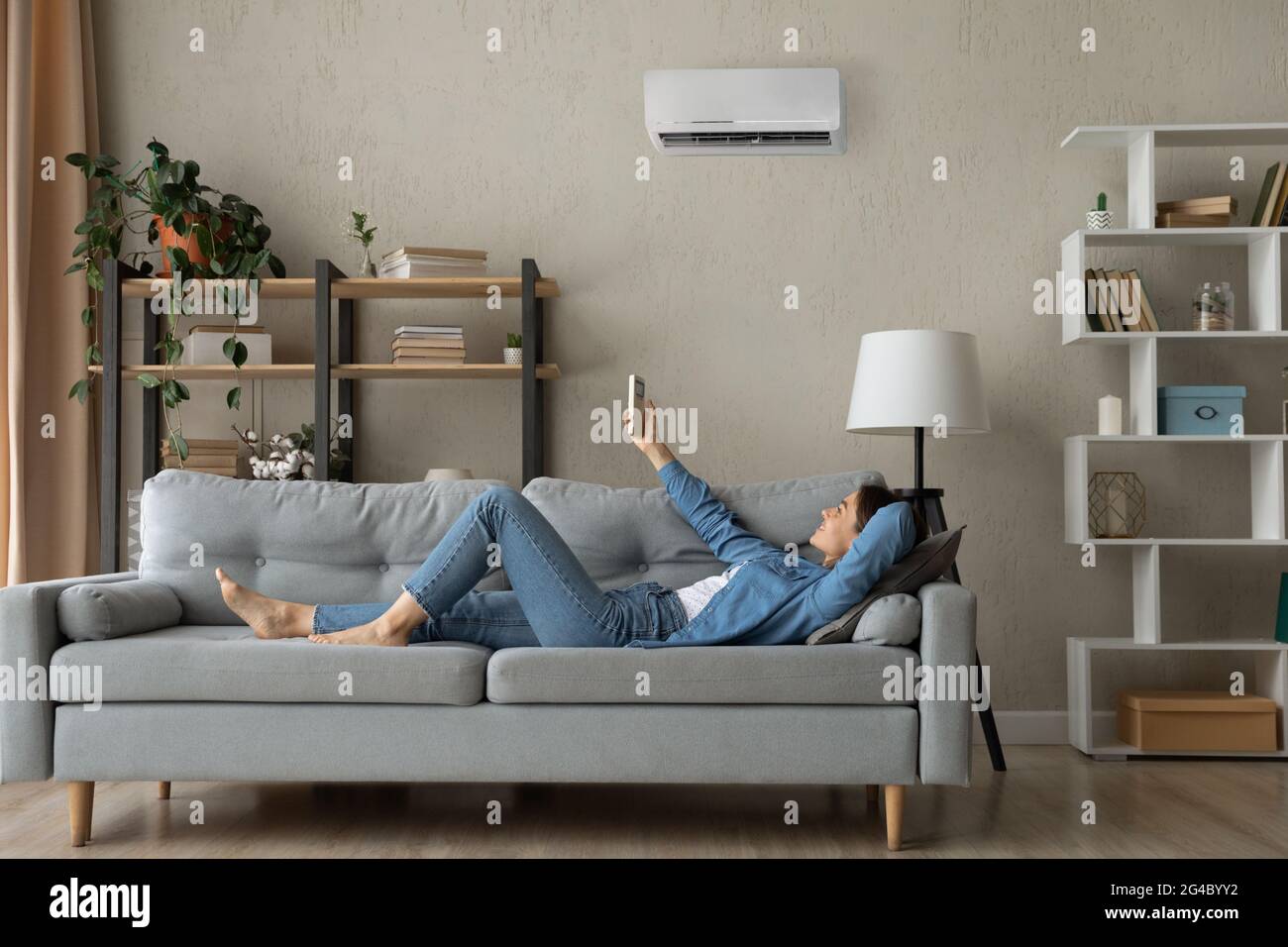 Relaxed young happy woman turning on air conditioner Stock Photo - Alamy
