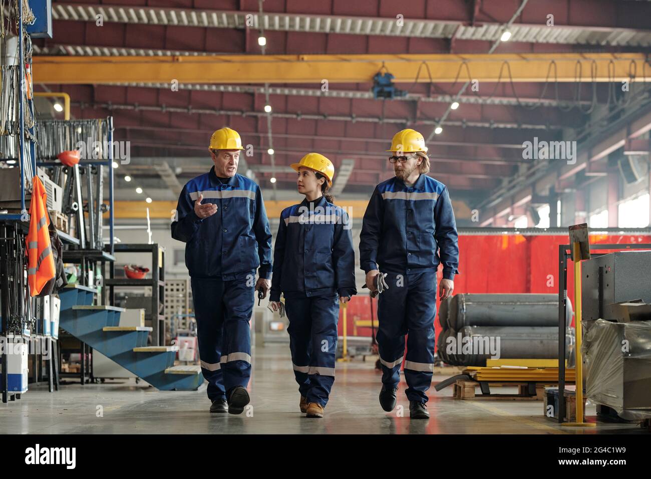 Mature factory foreman walking along workshop and gesturing hand while ...