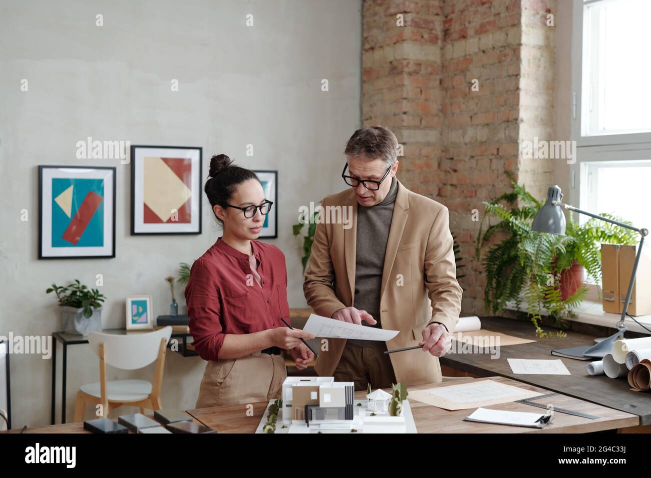 Chief architect in jacket standing at desk with 3D model of cottage ...