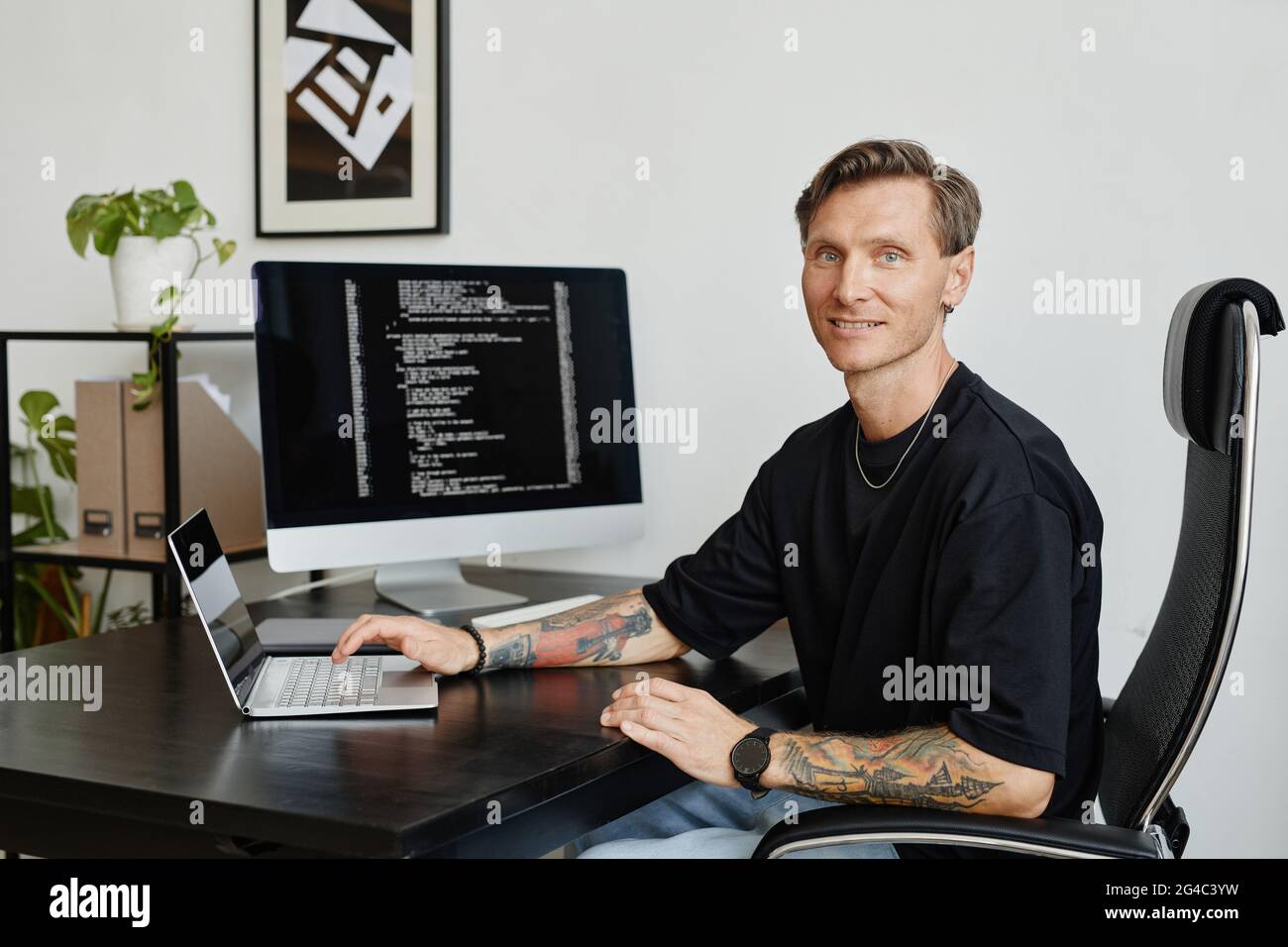 Portrait of mature computer programmer smiling at camera while working at the table with ...