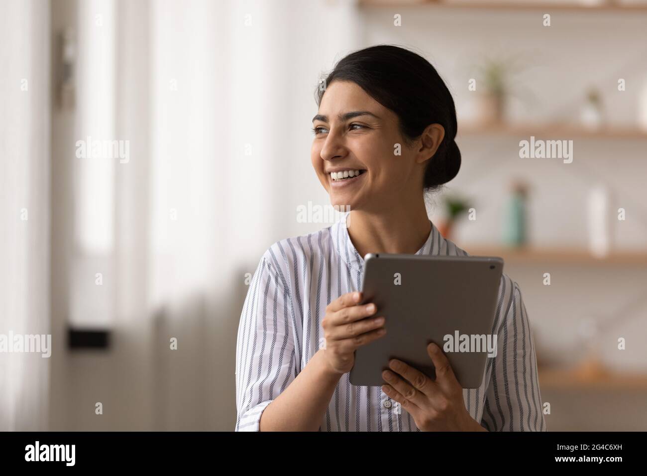 Smiling Indian woman use tablet look in distance Stock Photo - Alamy