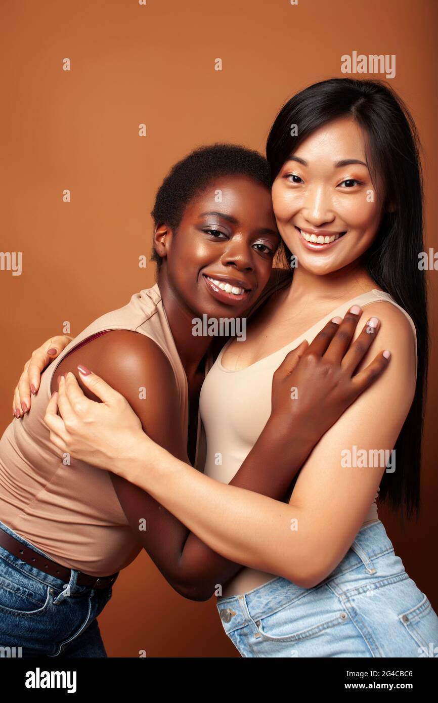 young pretty asian, afro woman posing cheerful together on brown ...