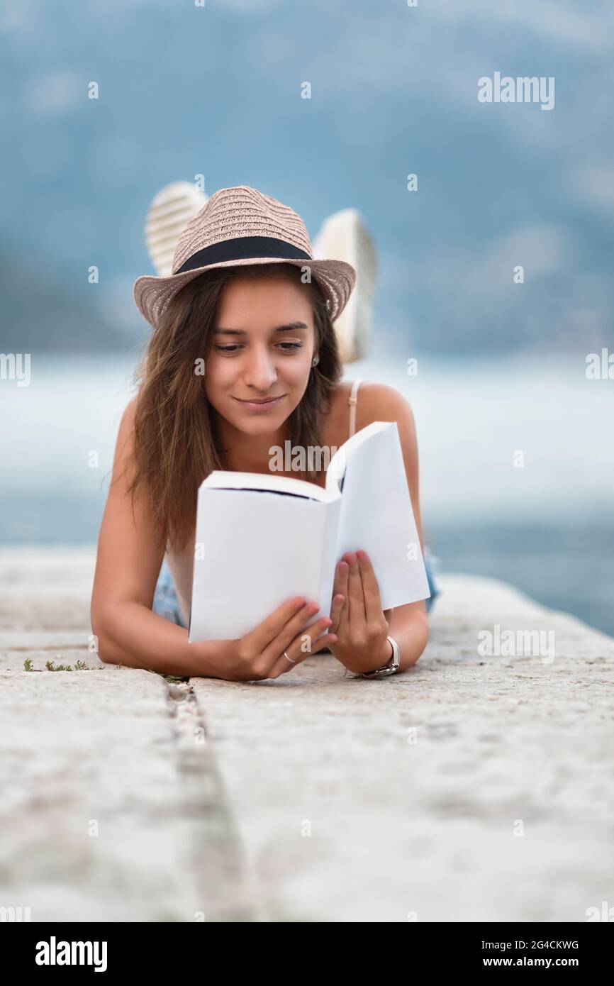 A young Caucasian female reading a book while resting on the beach ...