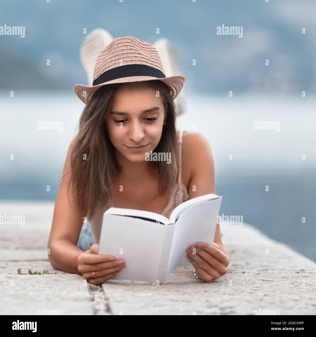 A young Caucasian female reading a book while resting on the beach ...