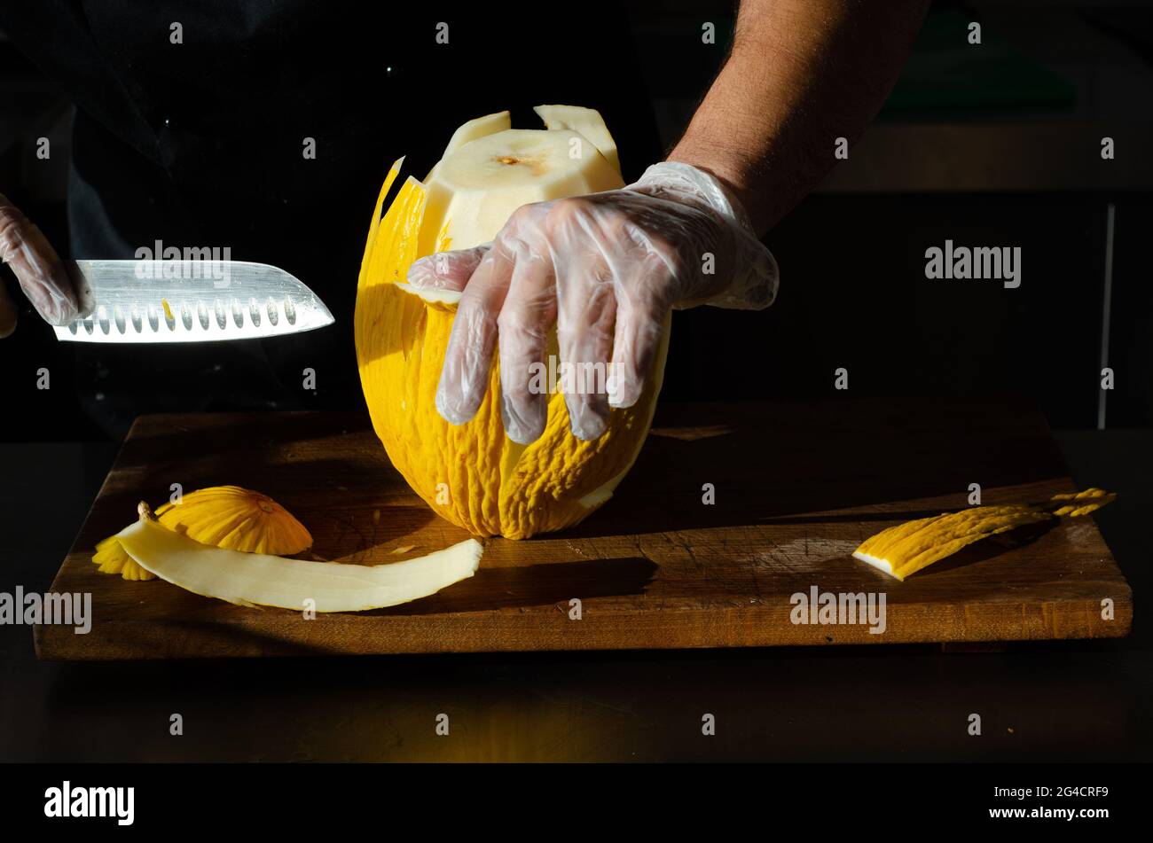 Closeup shot of a male cook peeling a yellow melon with knife on a ...