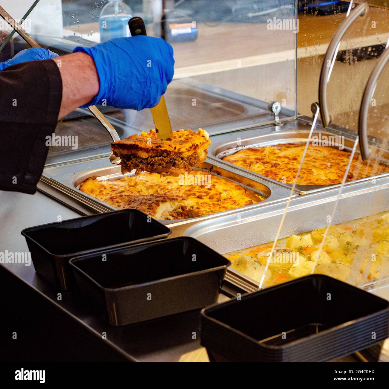 Chef wearing blue gloves and putting food in plastic black containers ...