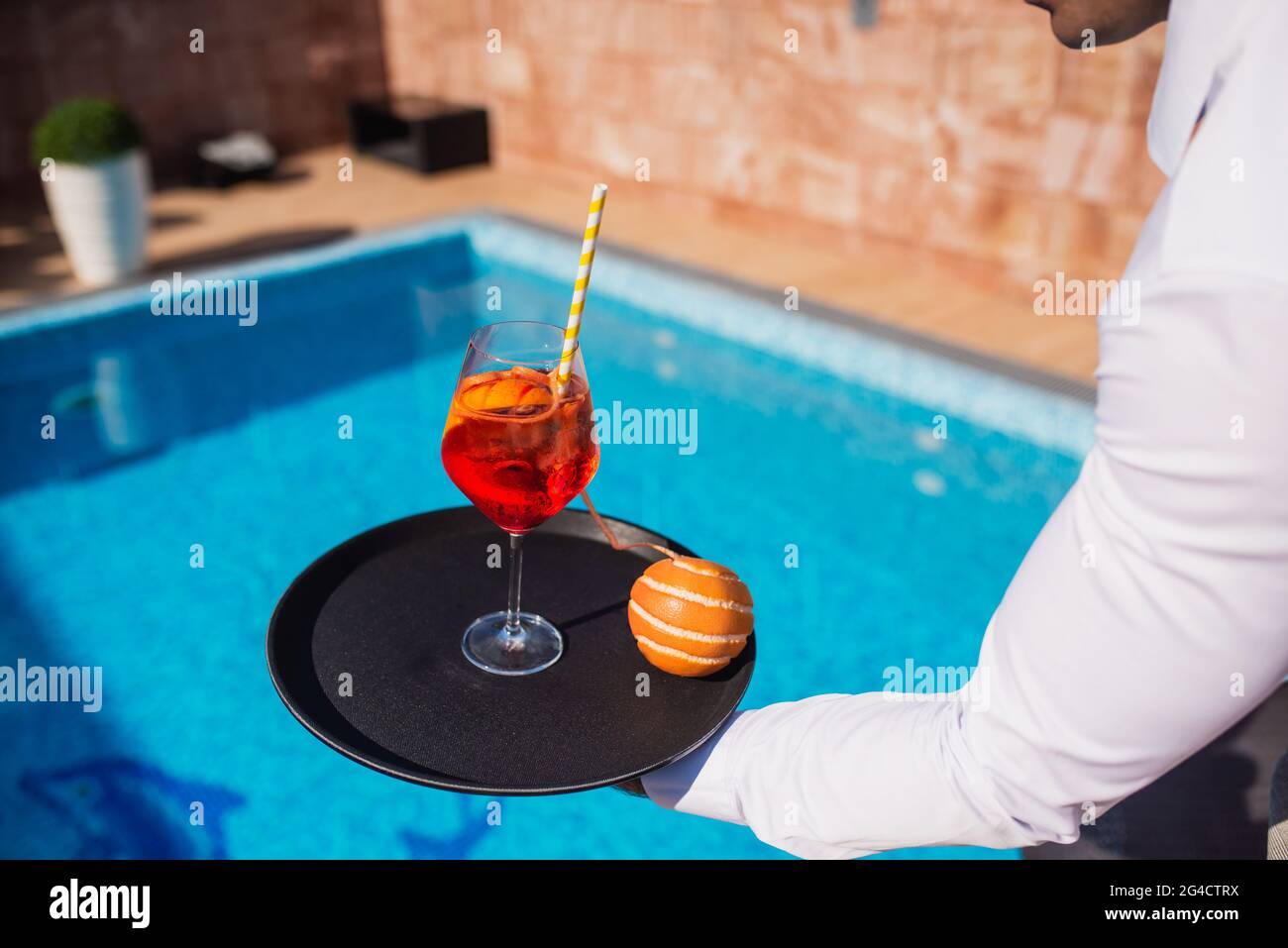 Waiter in white shirt serving red cocktail and orange at pool terrace ...