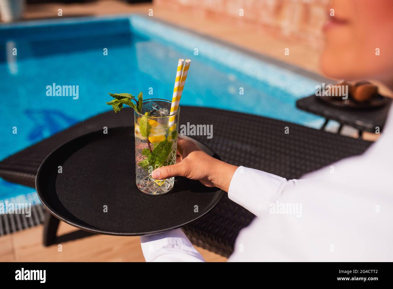 A waitress in a white shirt serves a mojito cocktail to guests by the ...