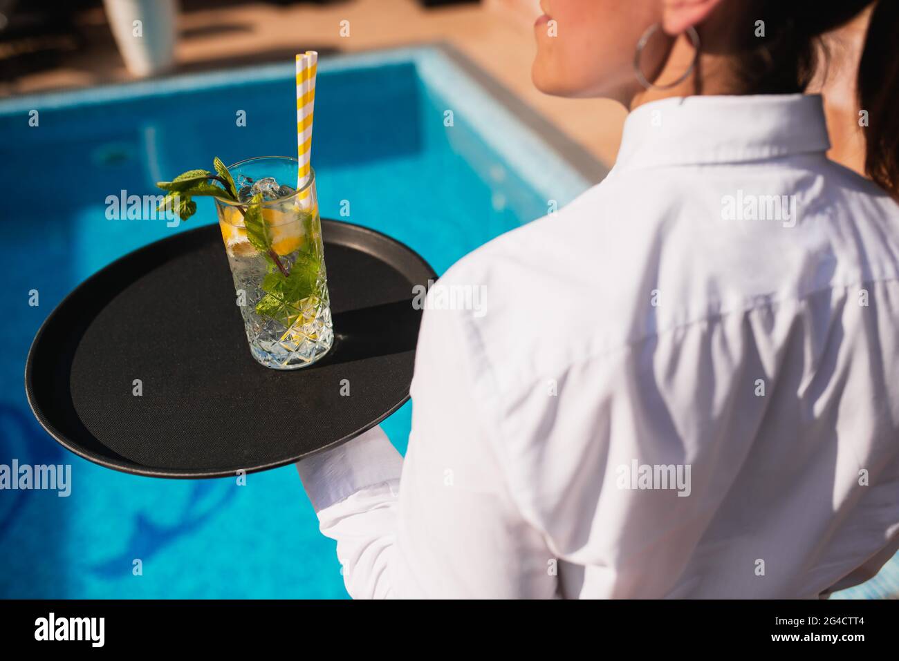 A female waitress serves a mojito cocktail on a tray by the pool. Crazy ...