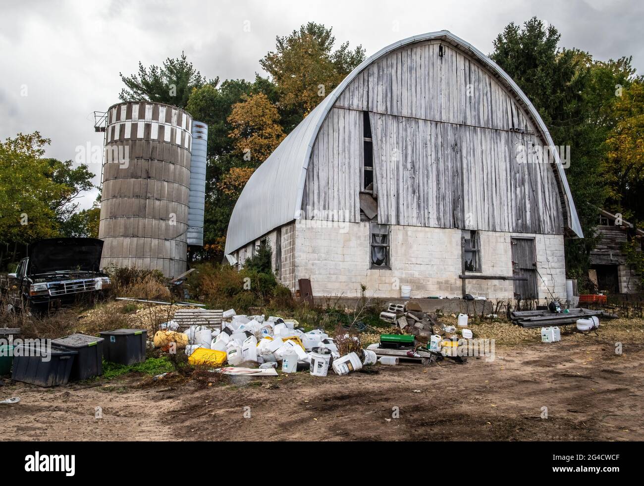 Old white abandoned barn and silo with various junk and an old truck ...
