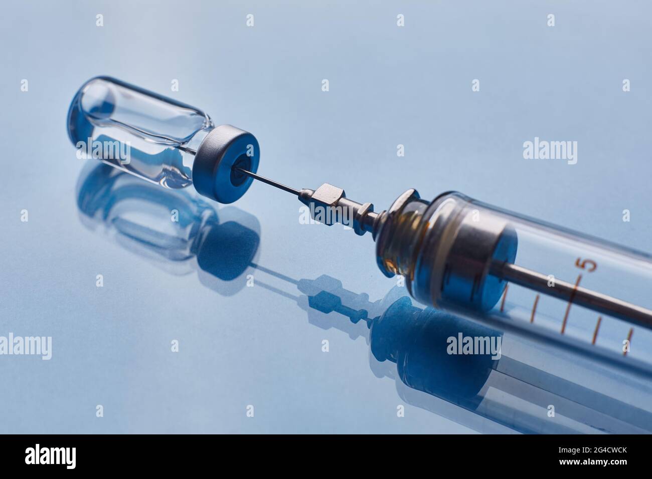 Glass vaccine vial and glass medical syringe on blue glass background ...