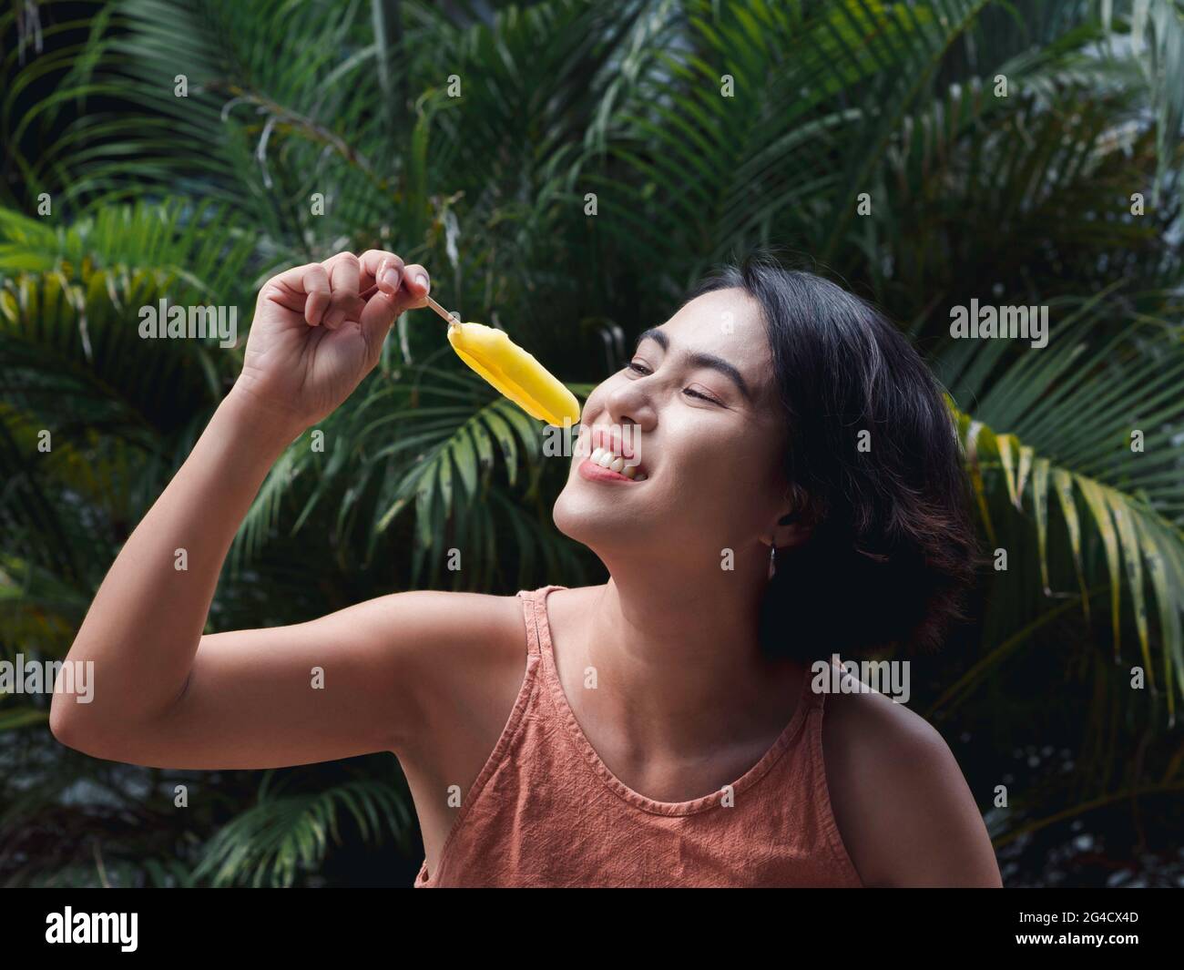 Woman eating popsicles. Happy beautiful Asian woman wearing casual pink ...