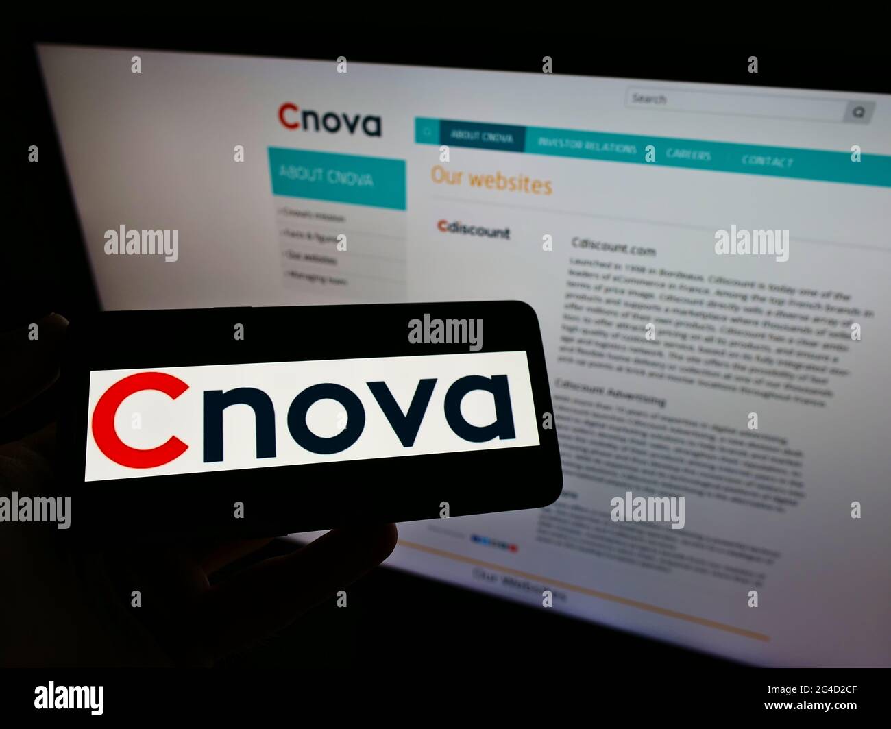 Person holding mobile phone with logo of e-commerce company Cnova N.V ...