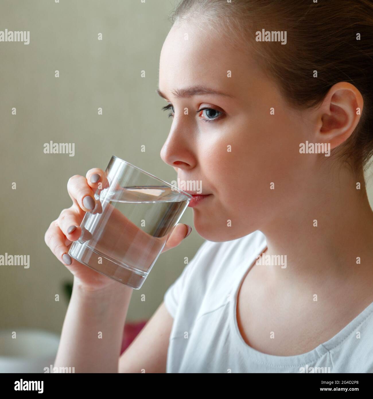 Young woman drinks glass of pure water in morning after waking up ...