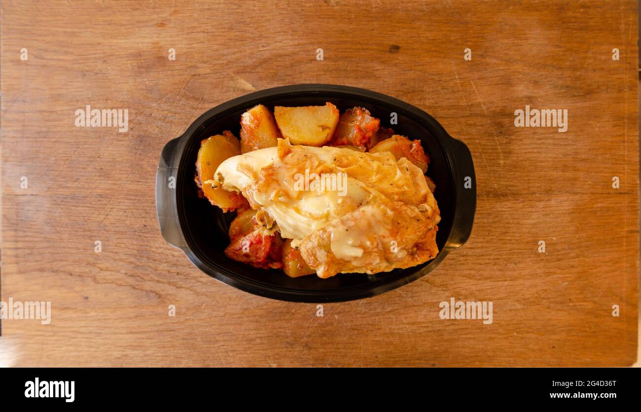 A top view of chicken with baked potatoes in a black plastic container ...