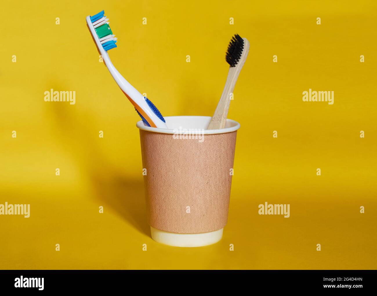 Wooden and plastic toothbrushes in a cardboard cup on a yellow ...