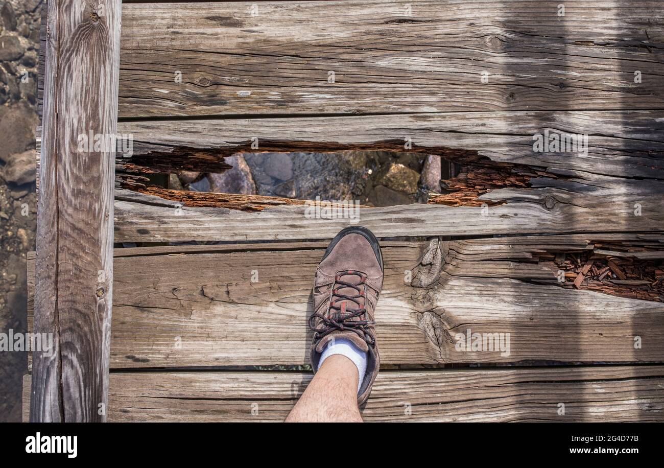 Trekker walking over broken wooden bridge. Visible river though the ...