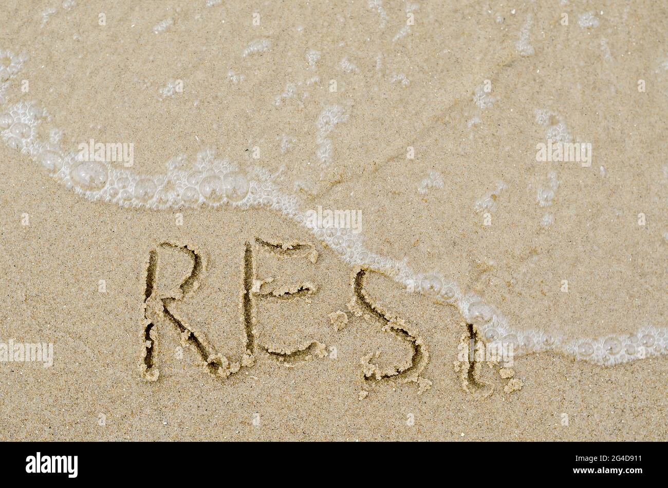 The wave washes away the word REST in the yellow sand. Handwritten word ...