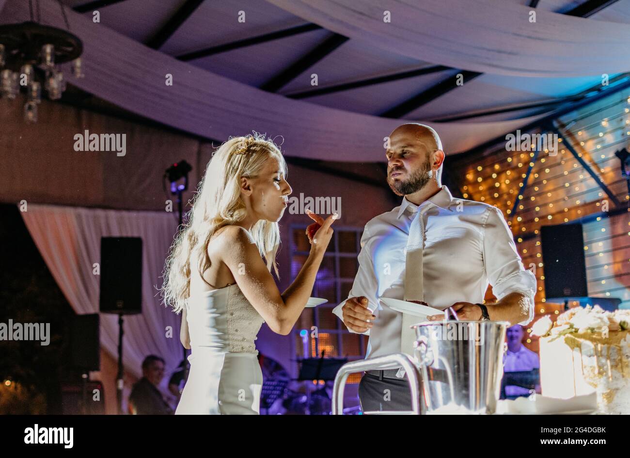 Bride and groom eating and feeding each other cake at wedding reception ...