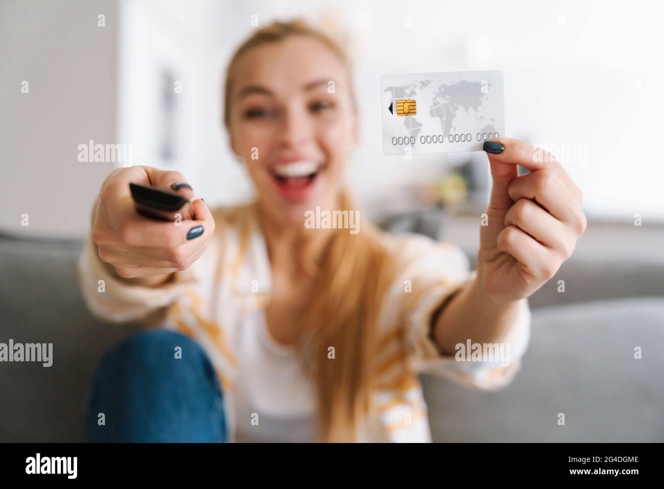 Excited woman showing credit card while watching tv with remote control ...