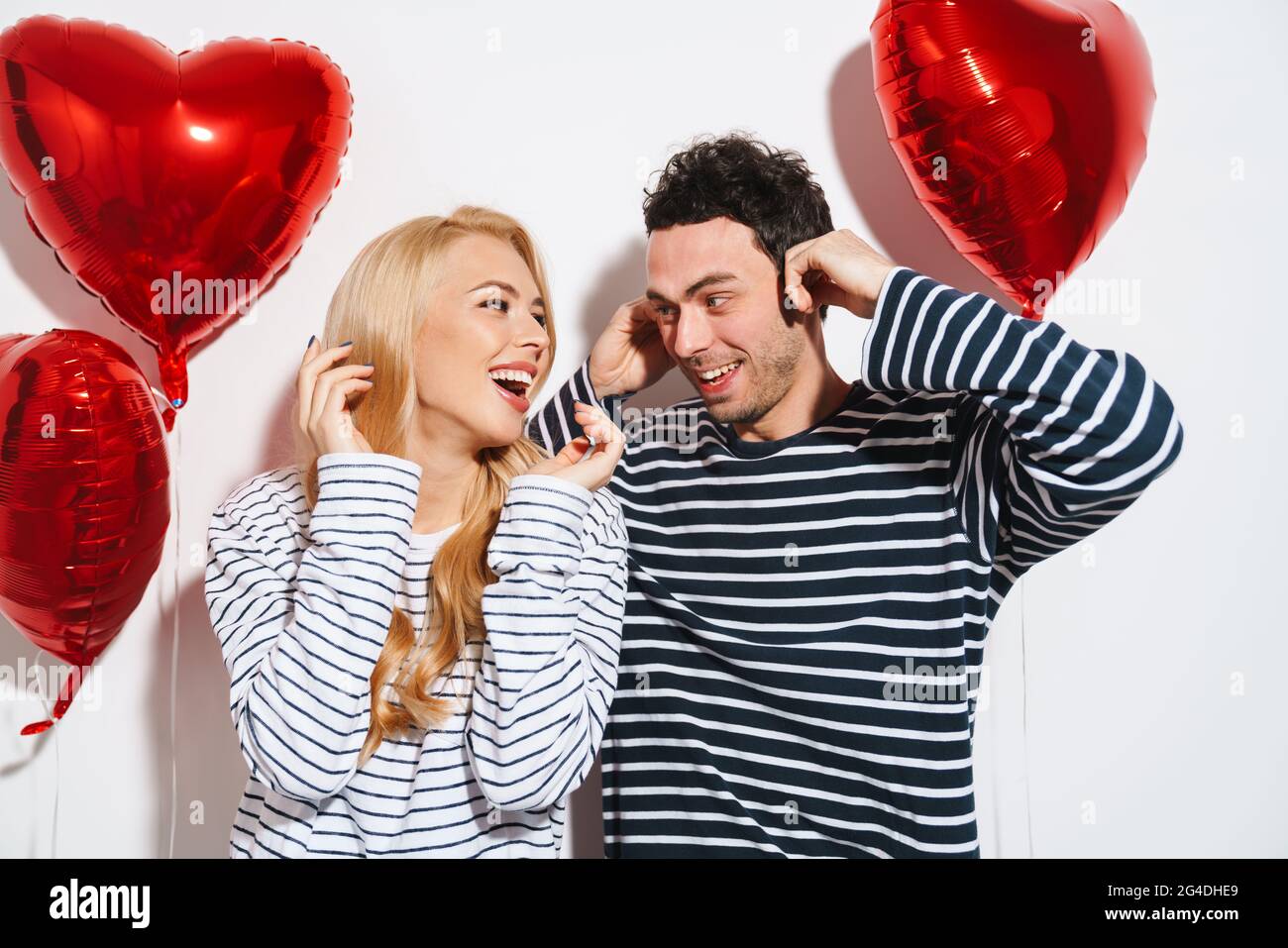 Joyful couple plugging their ears while posing with heart balloons ...