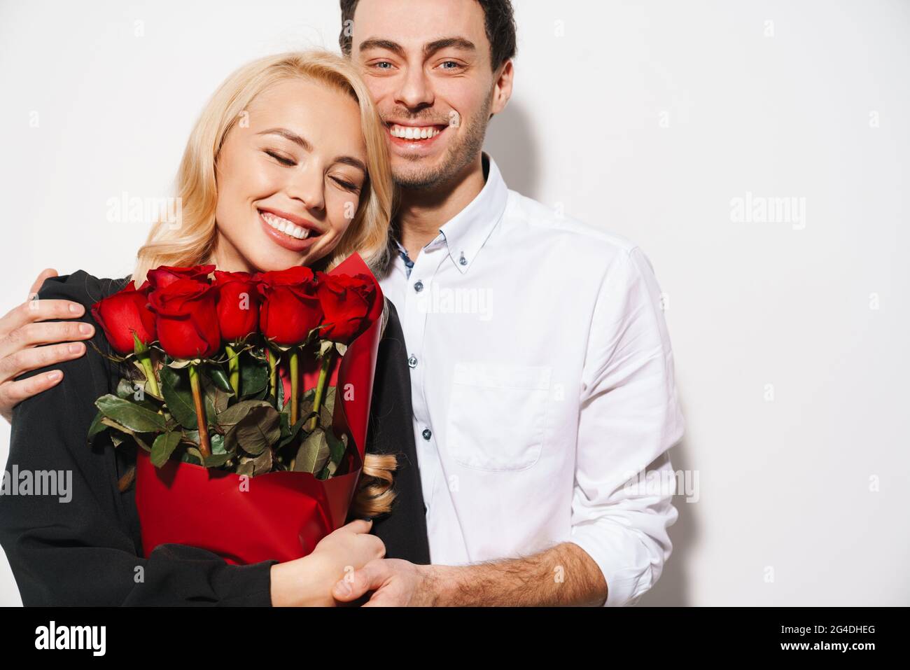 Happy romantic couple hugging while posing with red roses isolated over ...