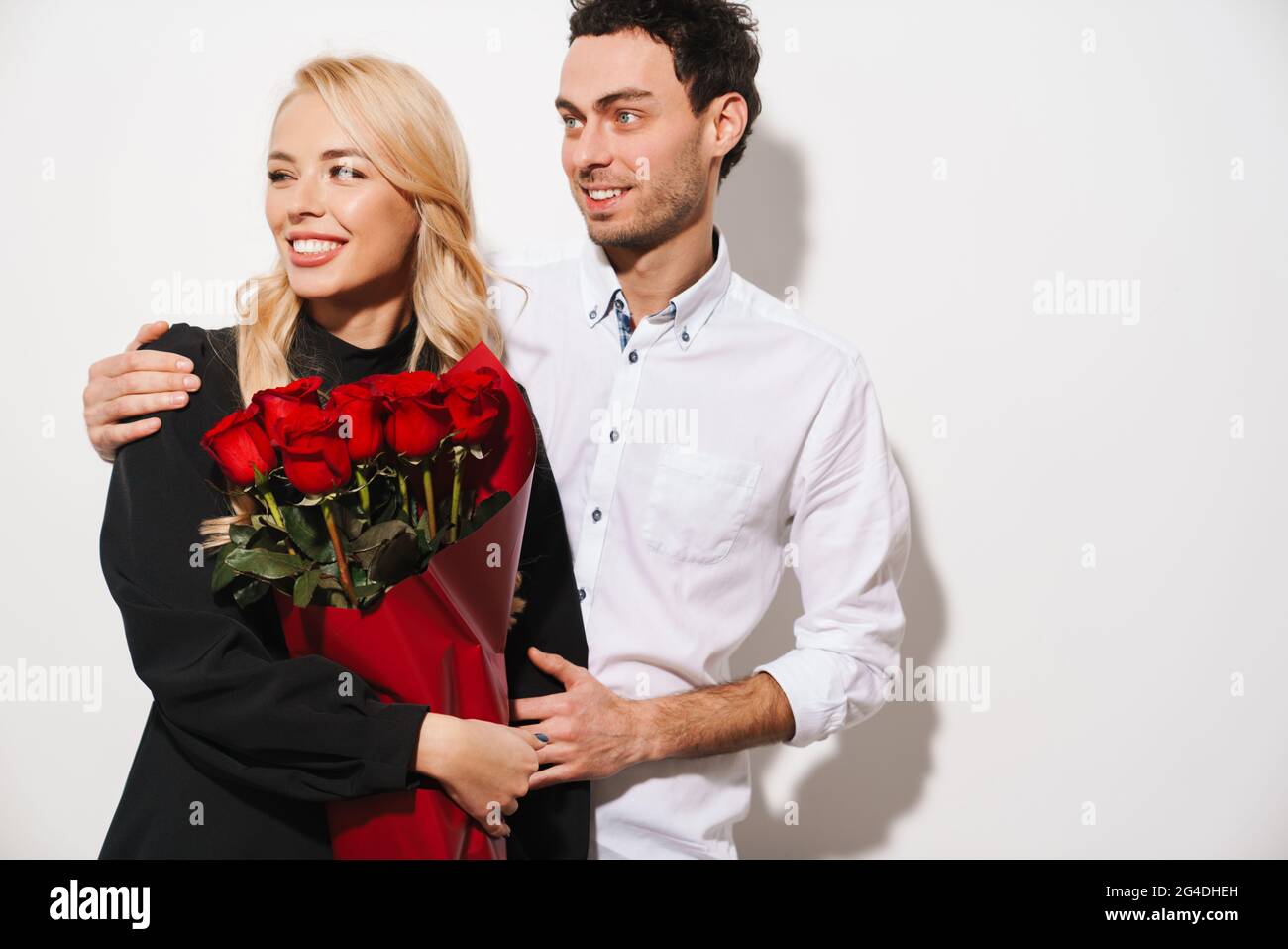 Happy romantic couple hugging while posing with red roses isolated over ...