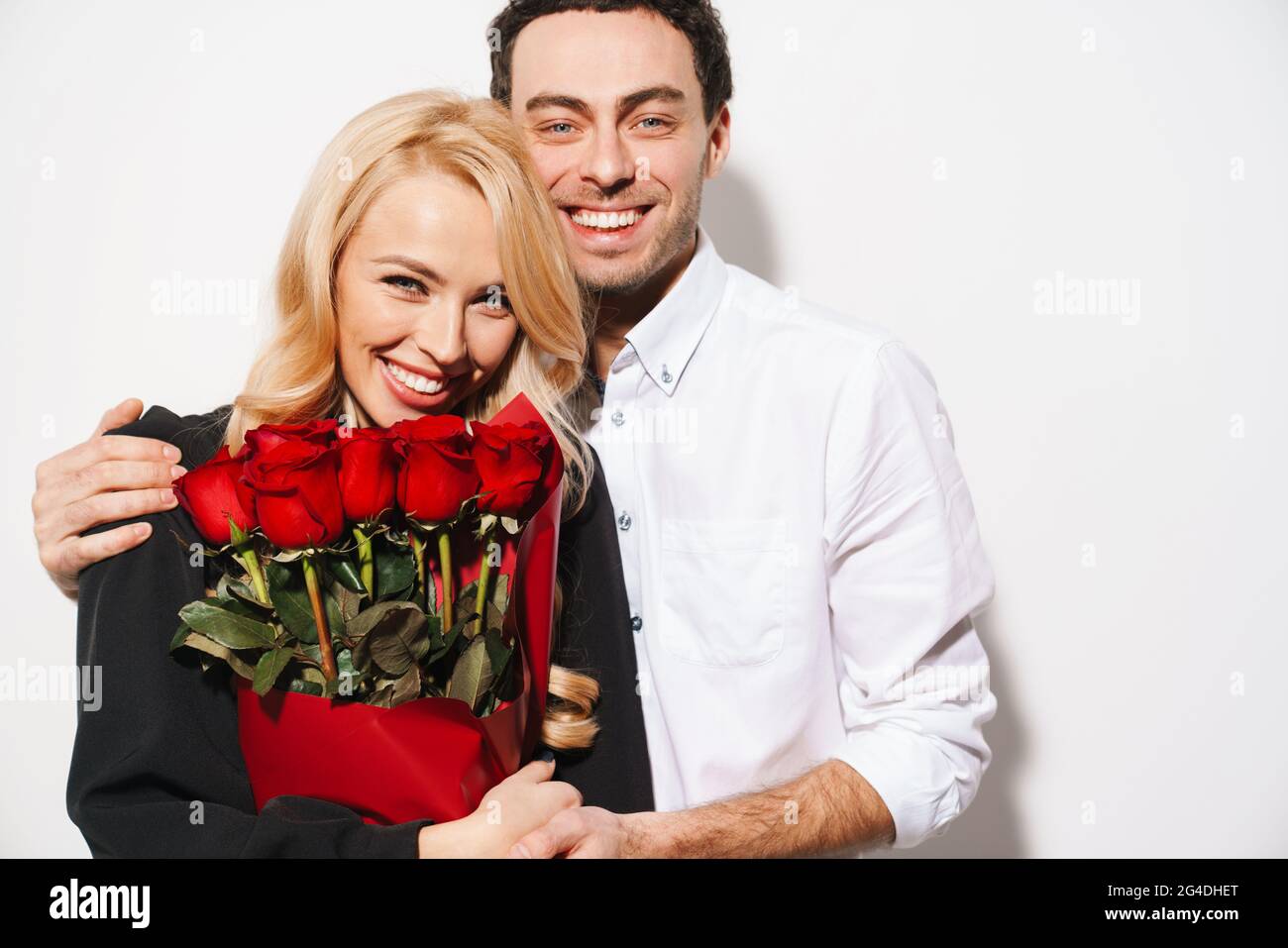 Happy romantic couple hugging while posing with red roses isolated over ...