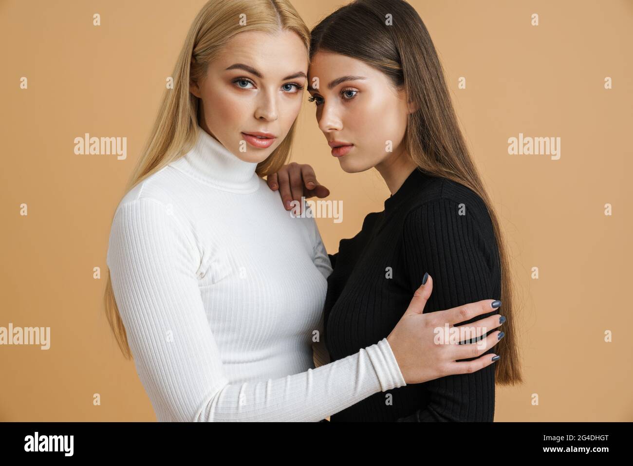 Beautiful two women hugging while posing on camera isolated beige ...