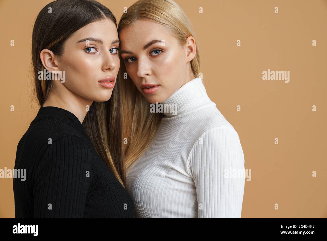 Beautiful young two women posing and hugging on camera isolated beige ...