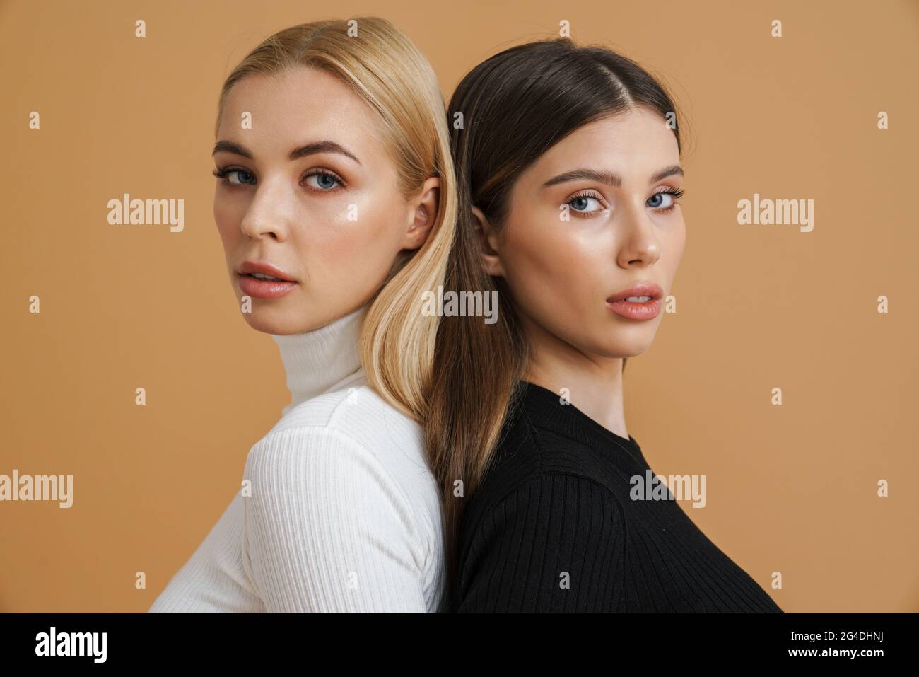 Beautiful two women posing back to back on camera isolated beige ...