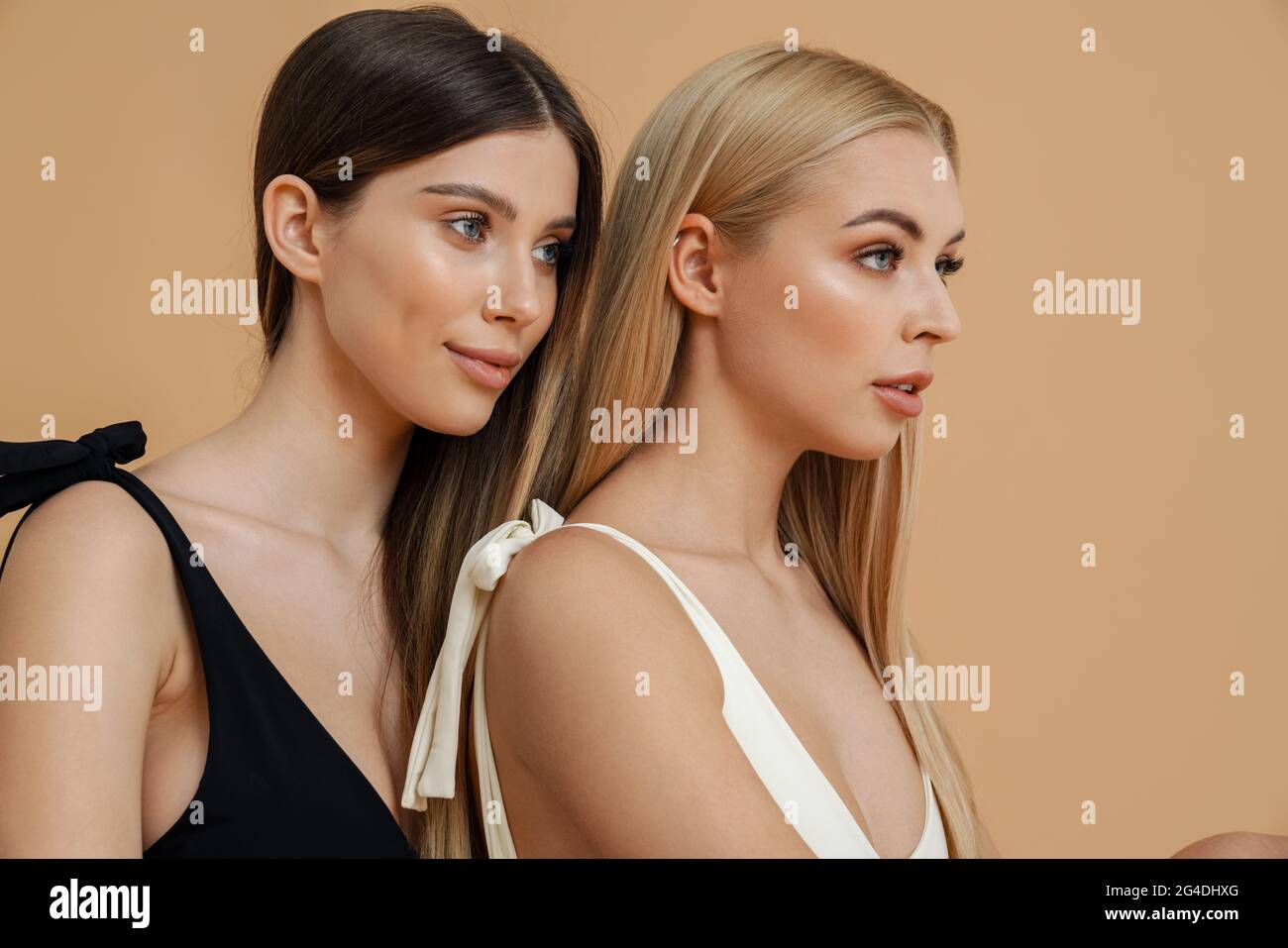 Sensual two women wearing swimsuits posing and looking aside isolated beige background Stock ...