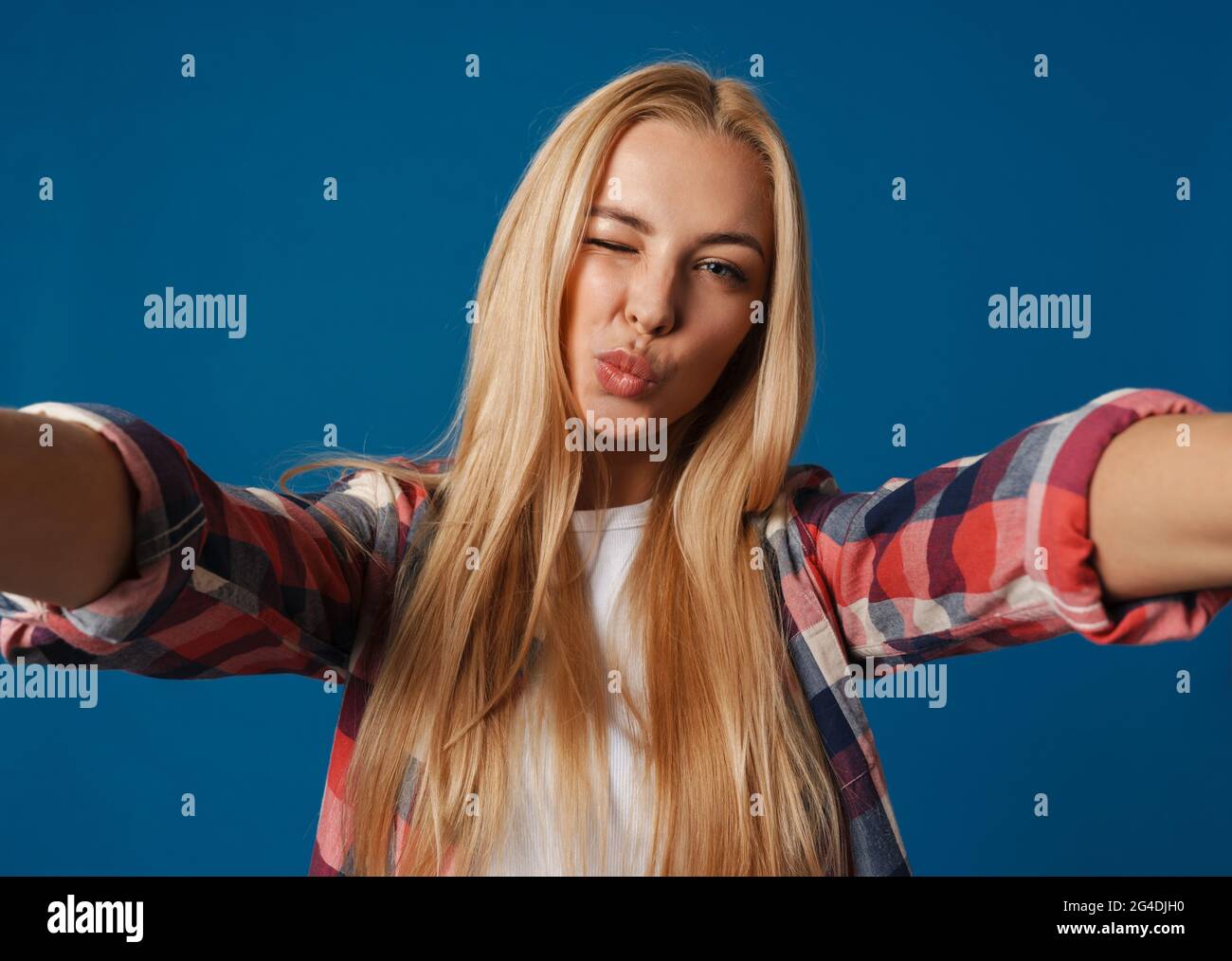 Happy blonde girl winking while taking selfie photo isolated over blue ...