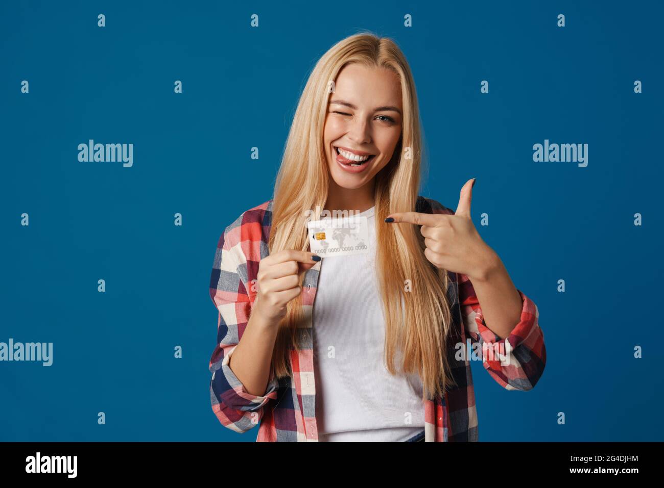 Blonde joyful woman winking and pointing finger at credit card isolated ...